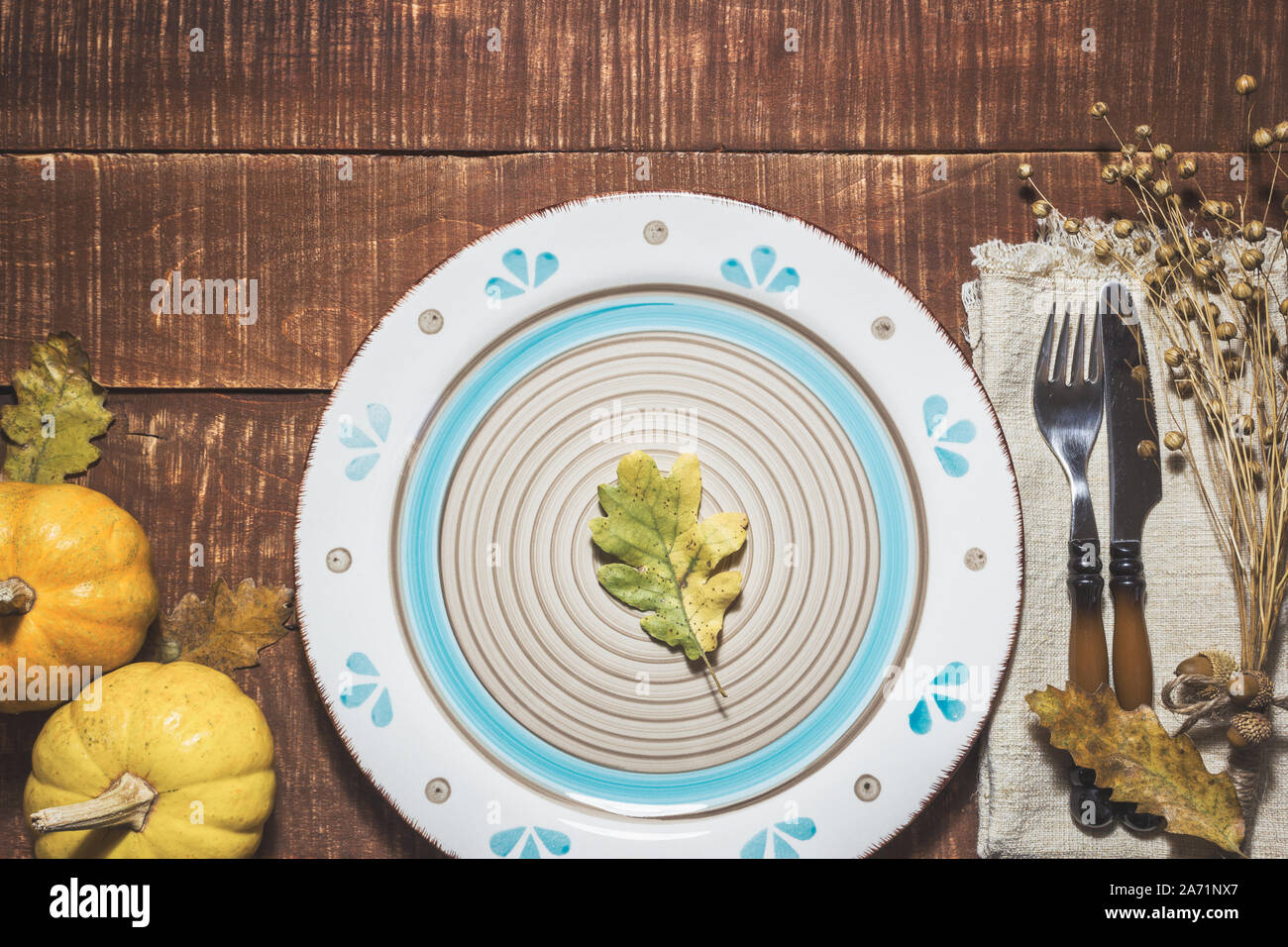 Rustic table setting for Thanksgiving diner with autumn leaves, acorns and pumpkins for ...