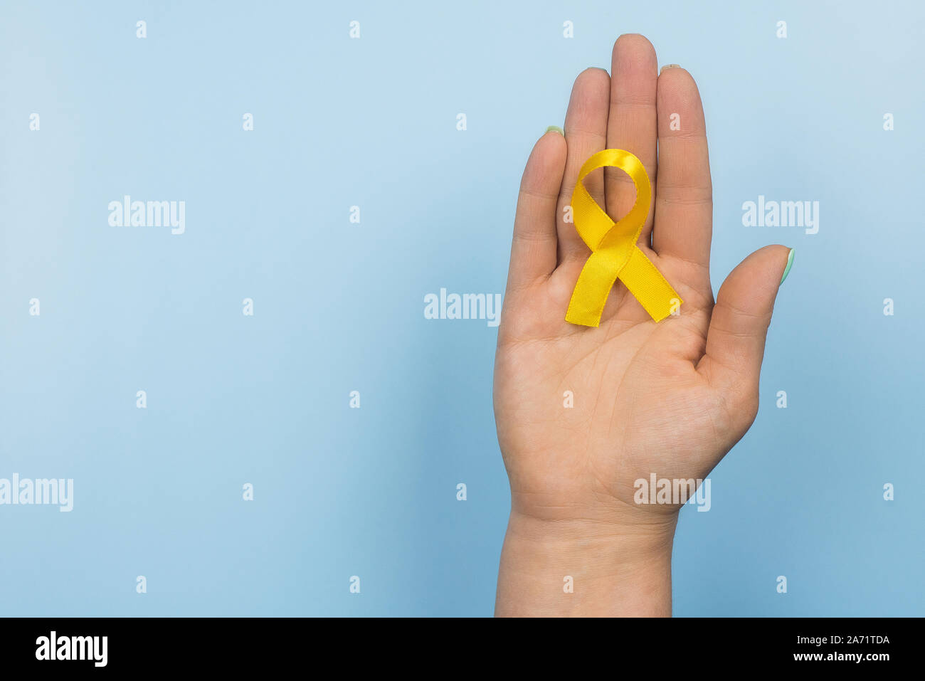 Yellow gold ribbon in the hand of a woman on a blue background ...