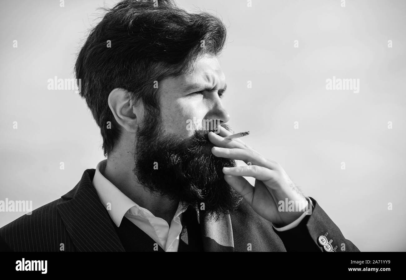 Bearded hipster smoking cigarette blue sky background. Guy enjoy ...