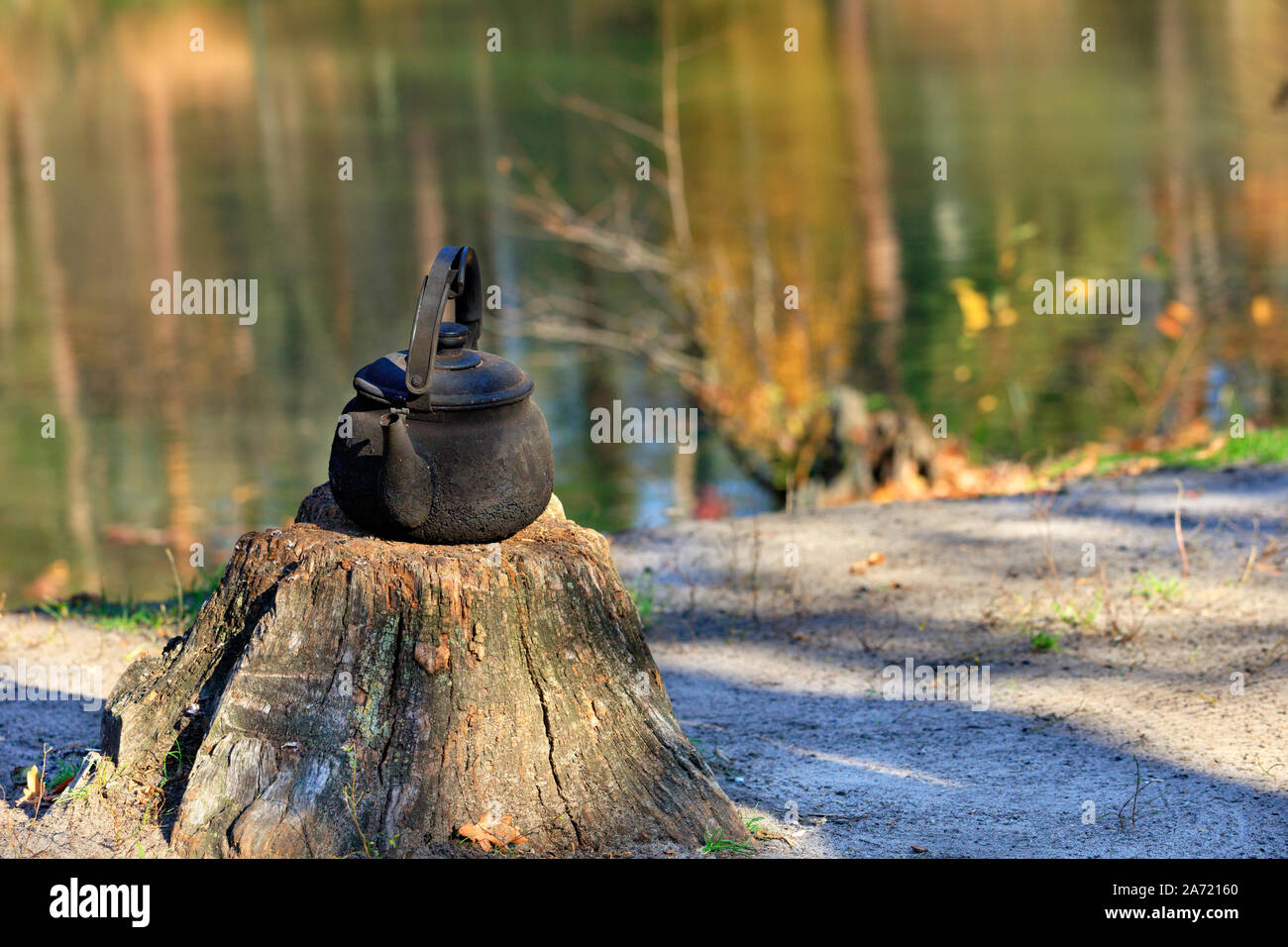 Metal burnt kettle stands on an old stump in the open air against a ...