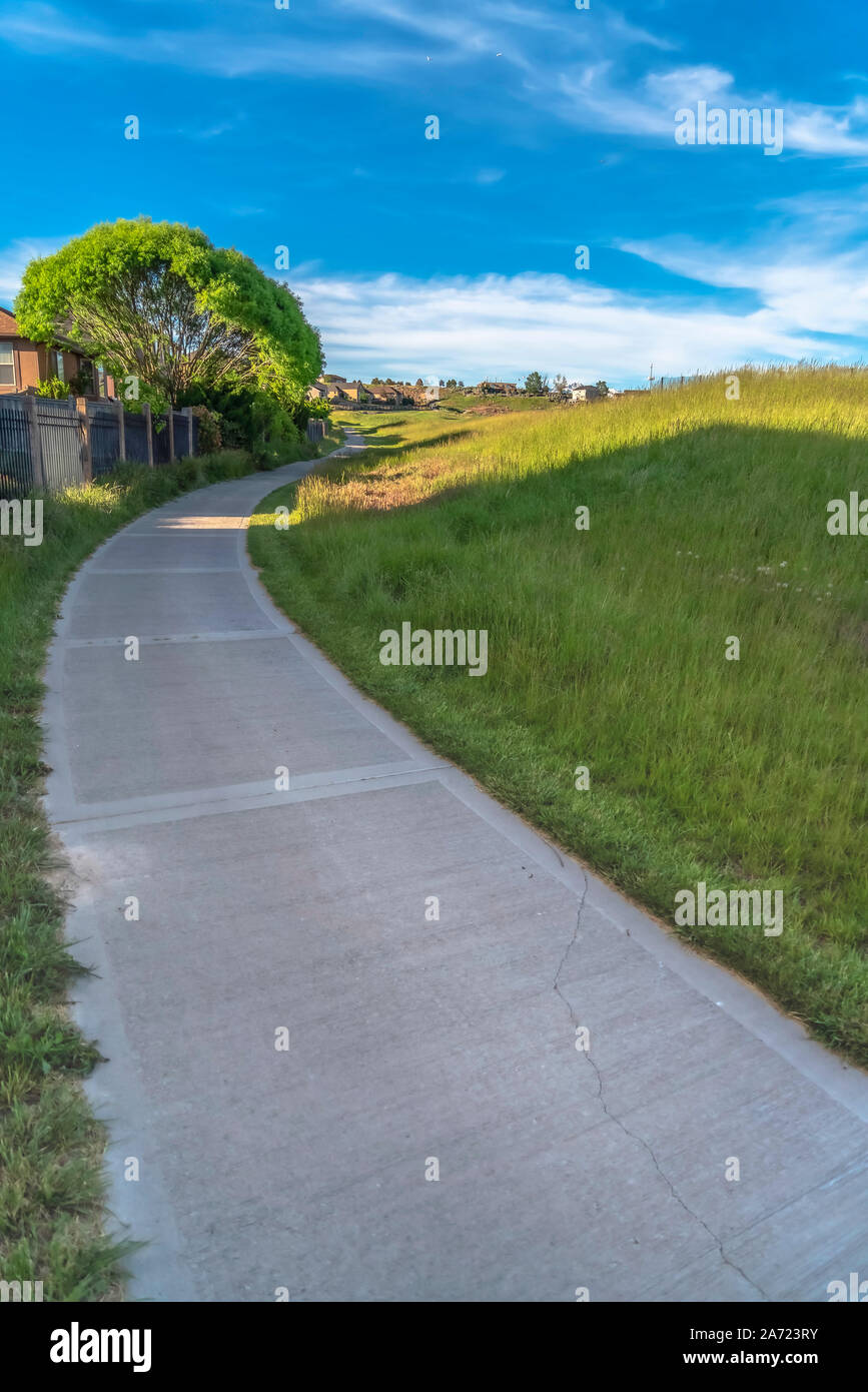 Concrete pathway on a grass covered hill under blue sky on a sunny day ...