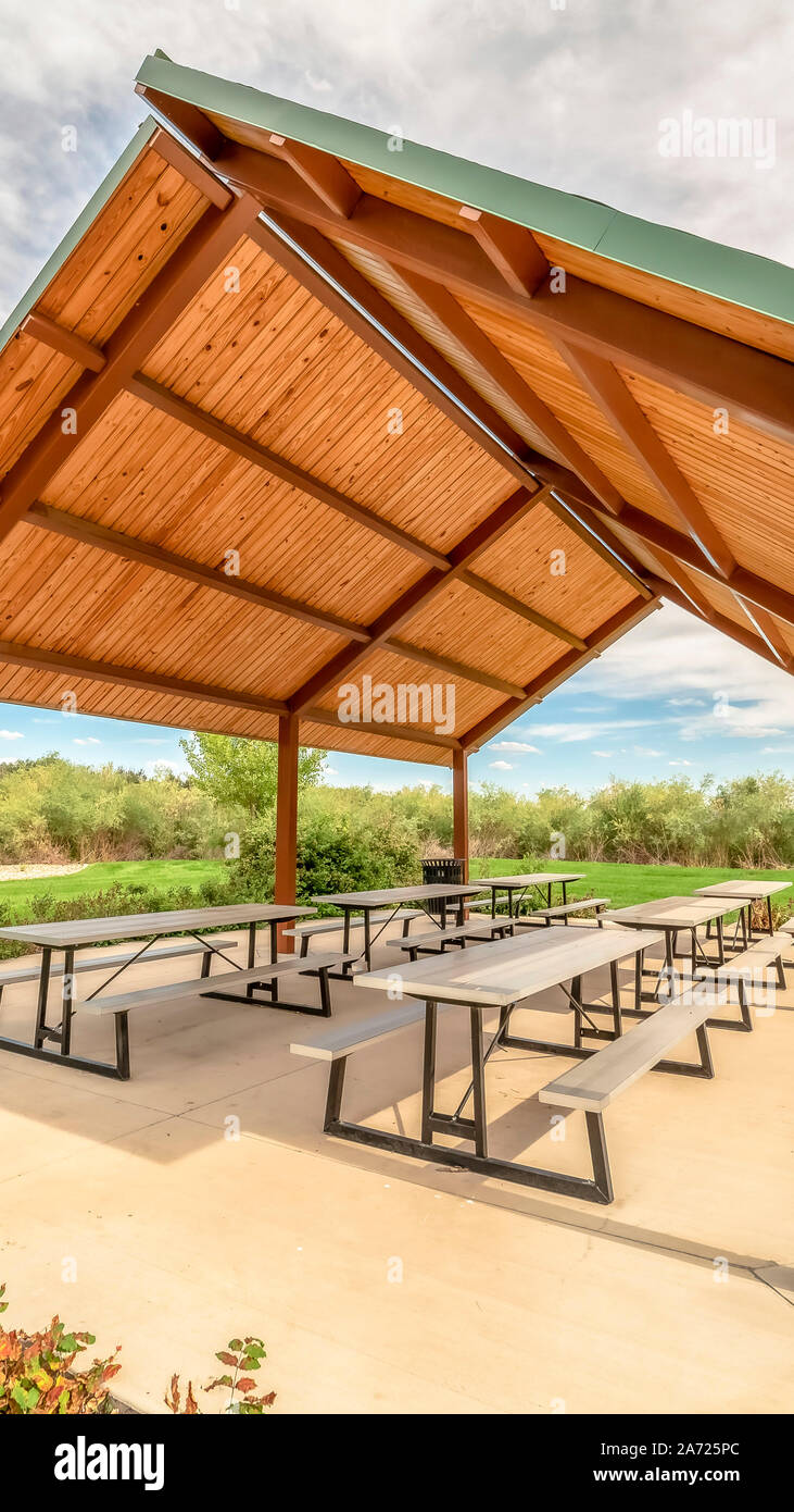 Vertical Sunny day at a park with view of tables and benches under a ...