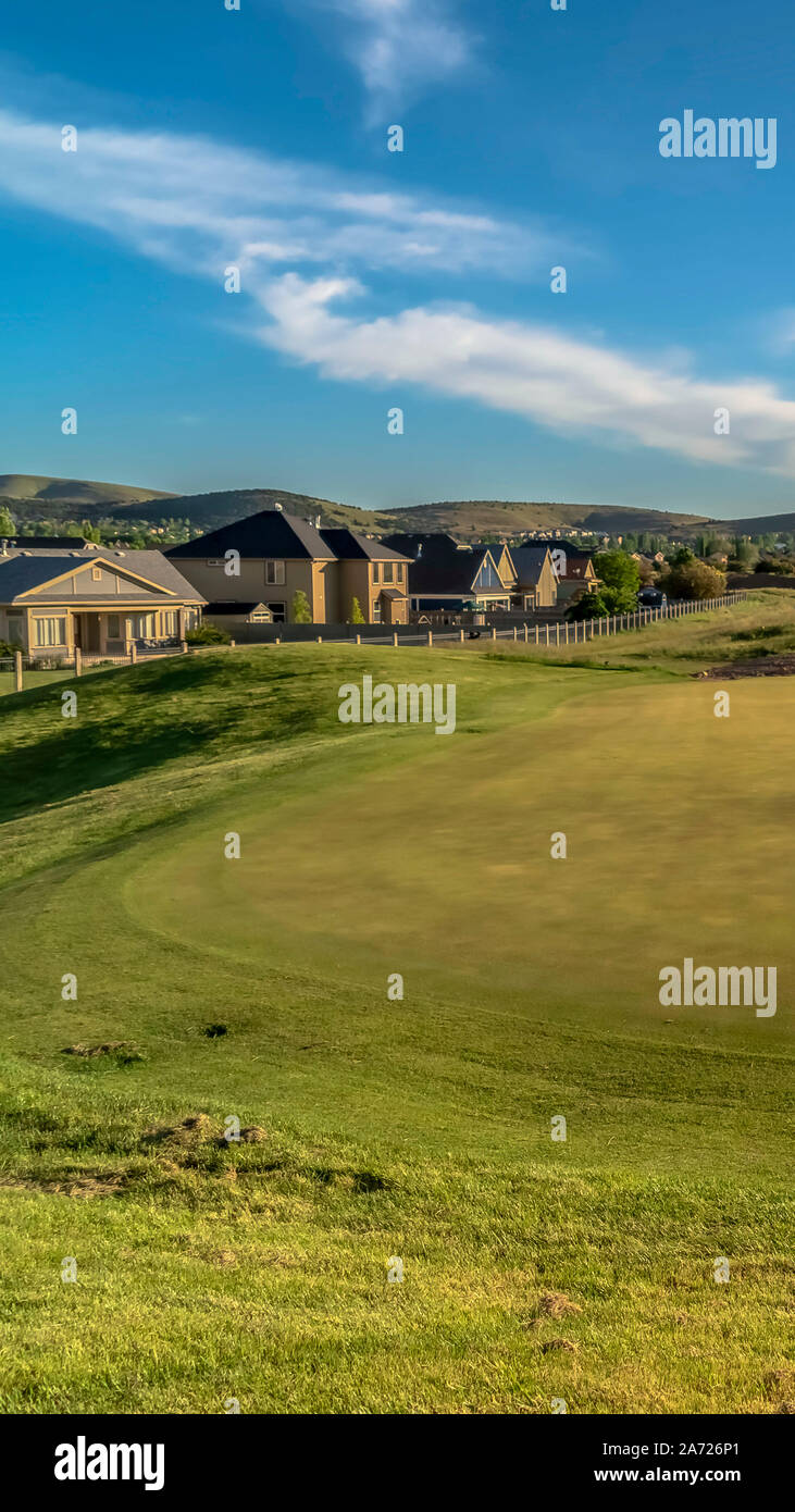 Vertical Scenic golf course landscape against houses and mountain under ...