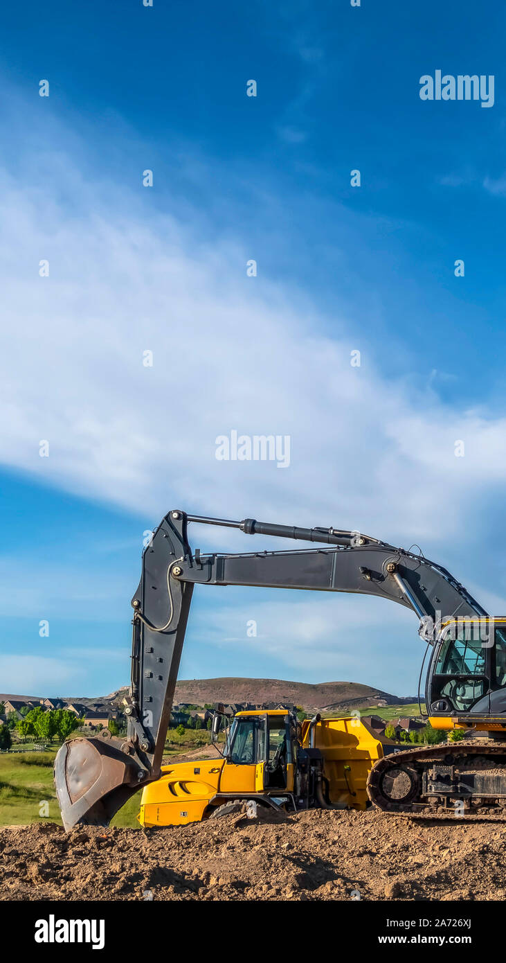 Vertical frame Excavator at a construction site with mountain homes and ...