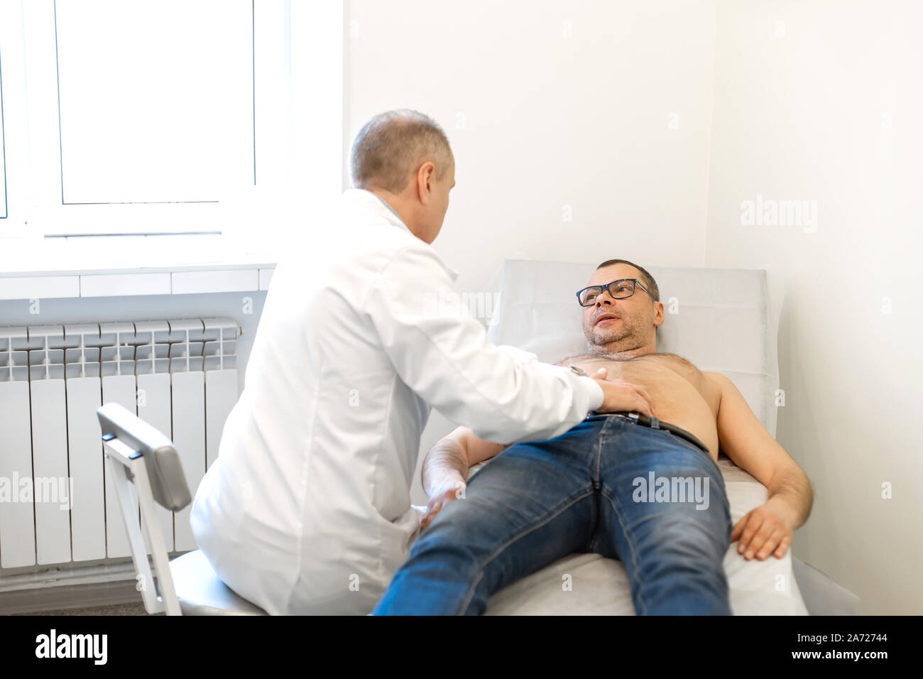 Doctor therapist probes the stomach of a male patient who is lying on a ...
