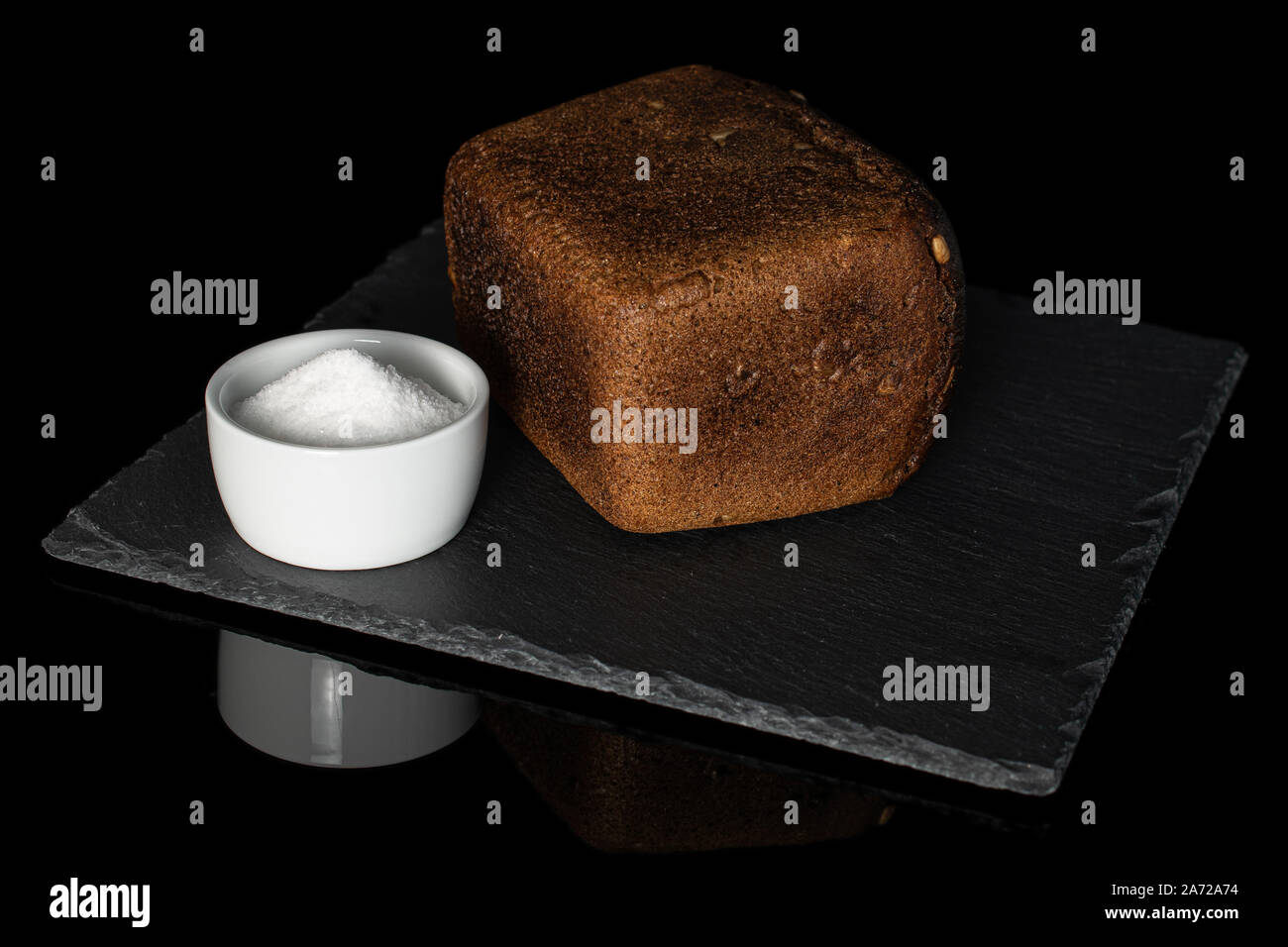 One whole fresh baked dark bread on grey stone with pinch of salt ...