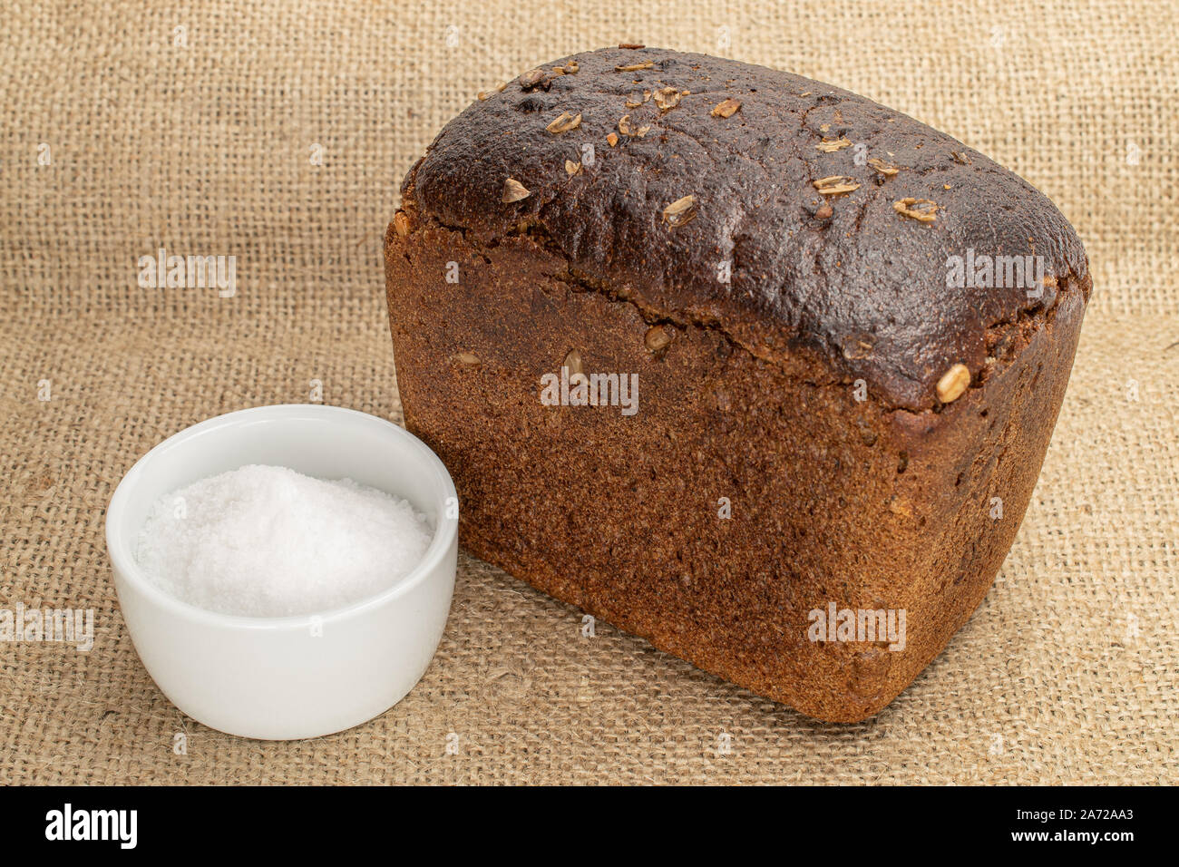 One whole fresh baked dark bread with pinch of salt on jute cloth Stock ...