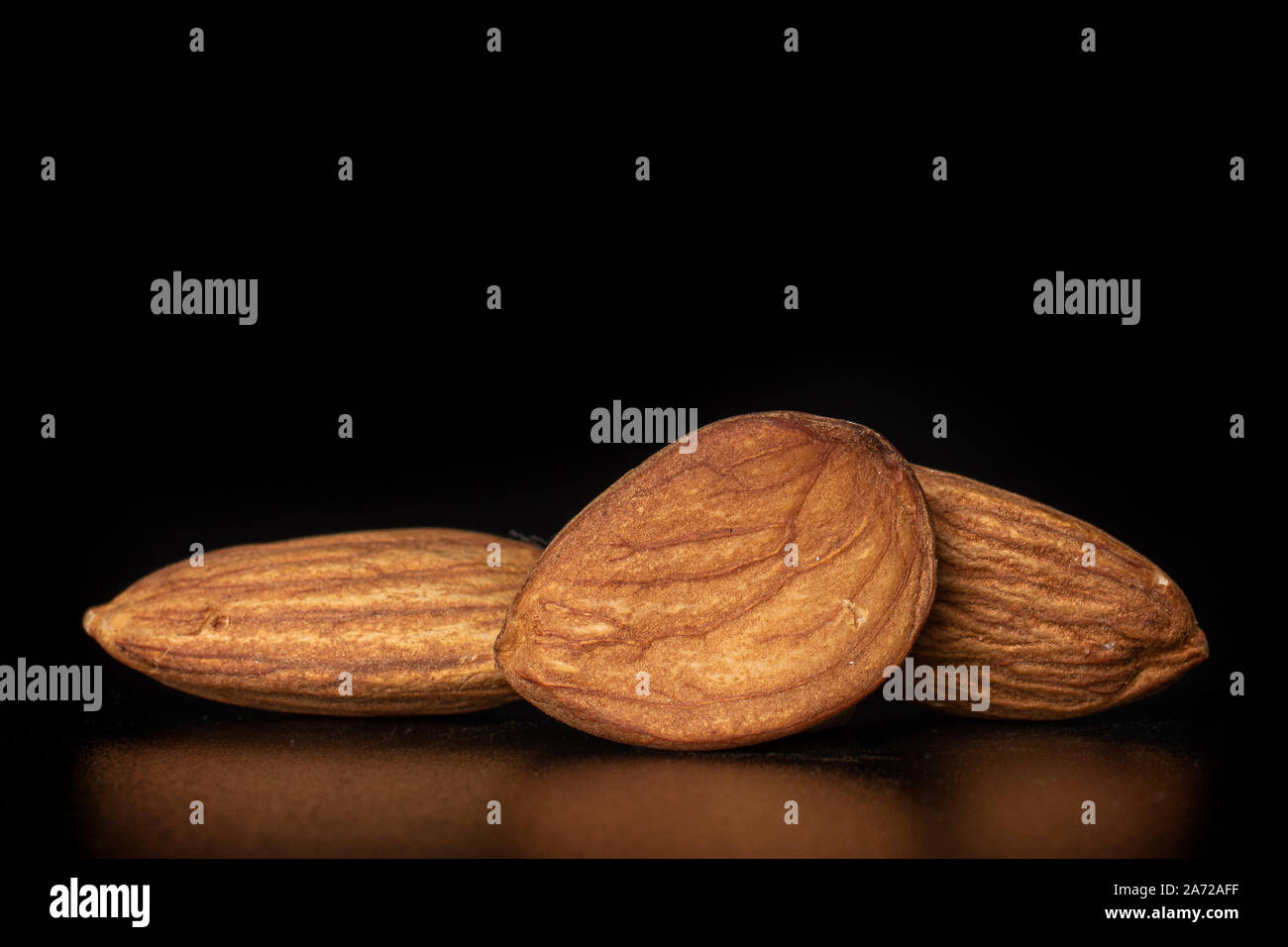 Group of three whole peeled almond nuts isolated on black glass Stock ...