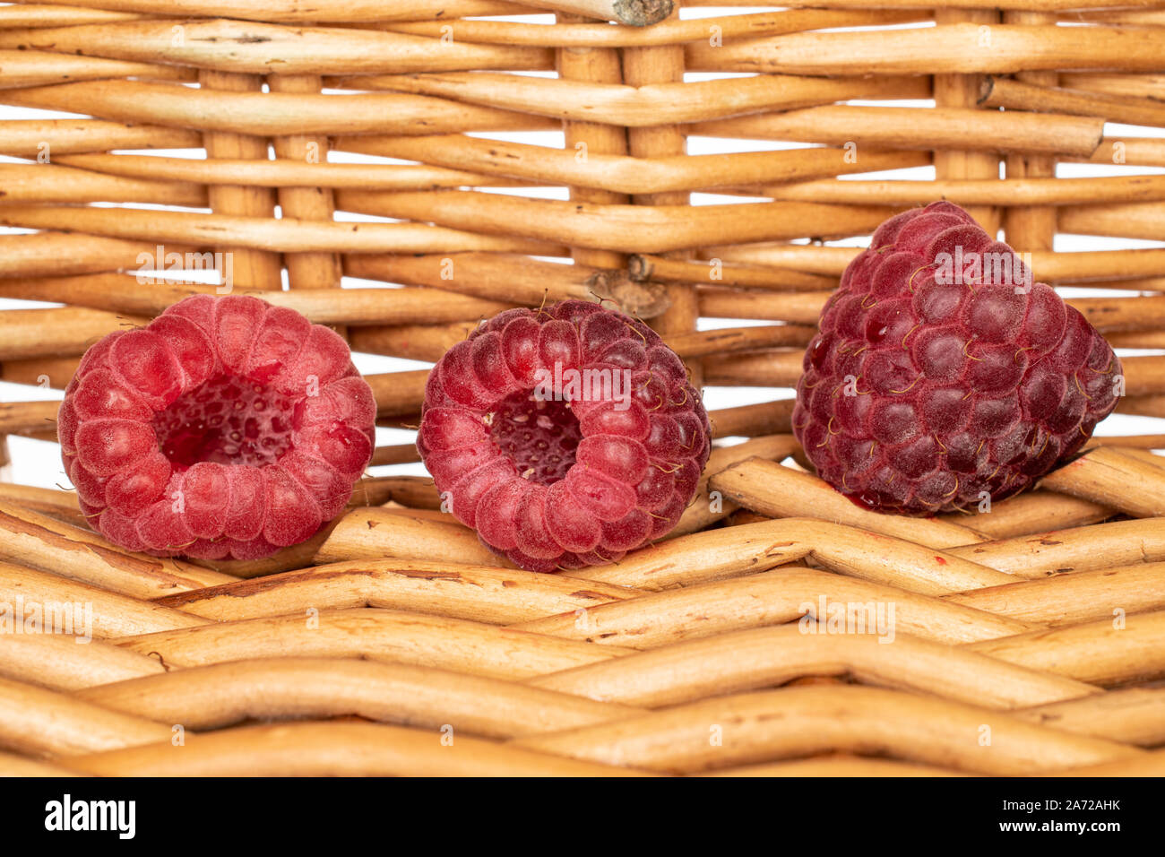 Group of three whole fresh crimson raspberry with braided rattan behind ...