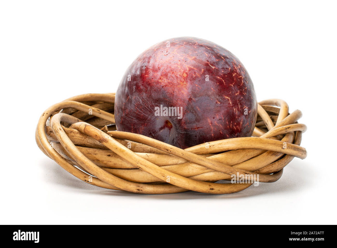 One whole fresh red plum in wiker nest isolated on white background ...