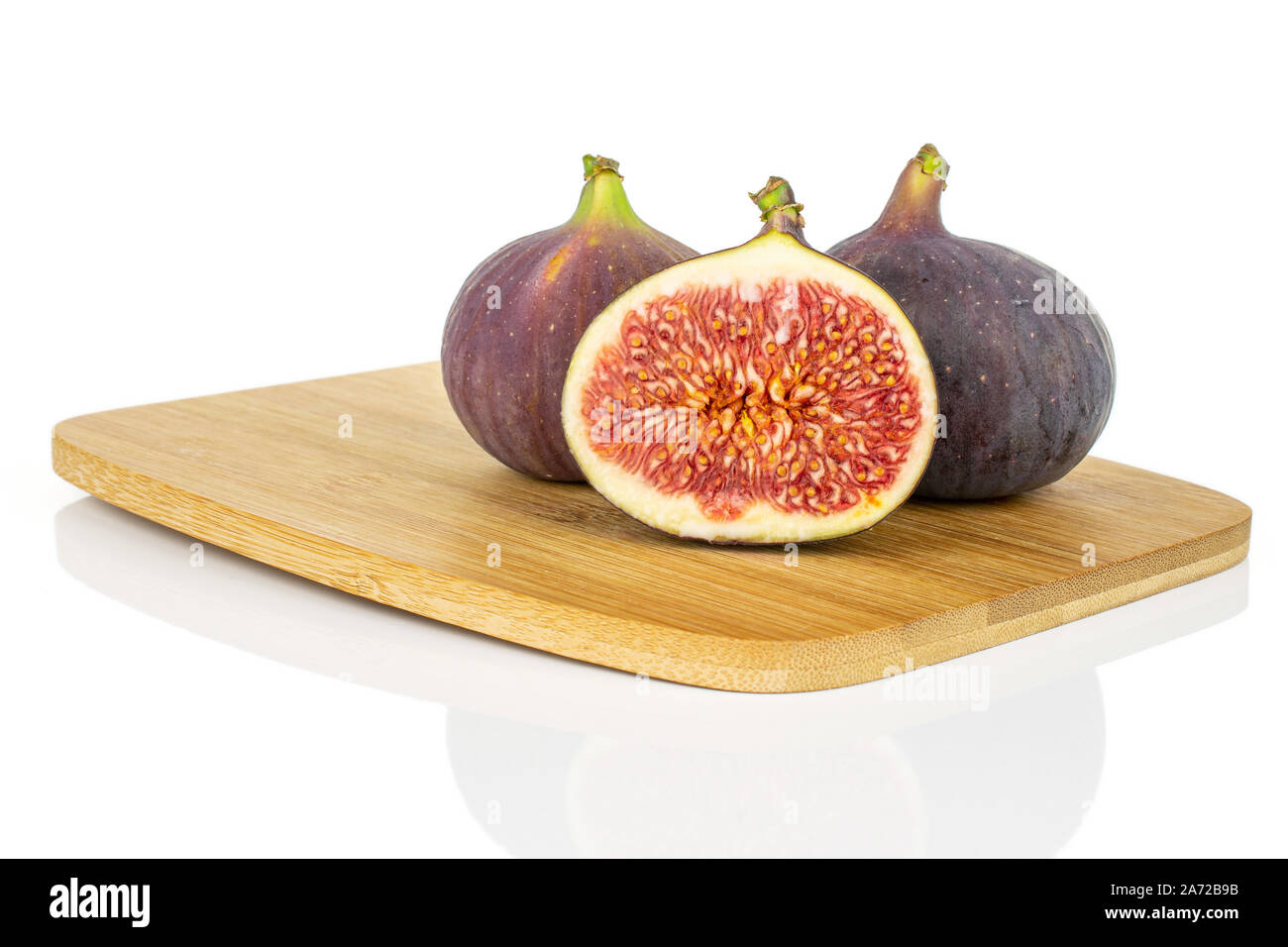 Group of two whole one half of fresh purple fig on bamboo cutting board ...