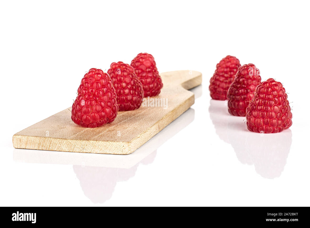 Group of six whole fresh red raspberry on small wooden cutting board ...
