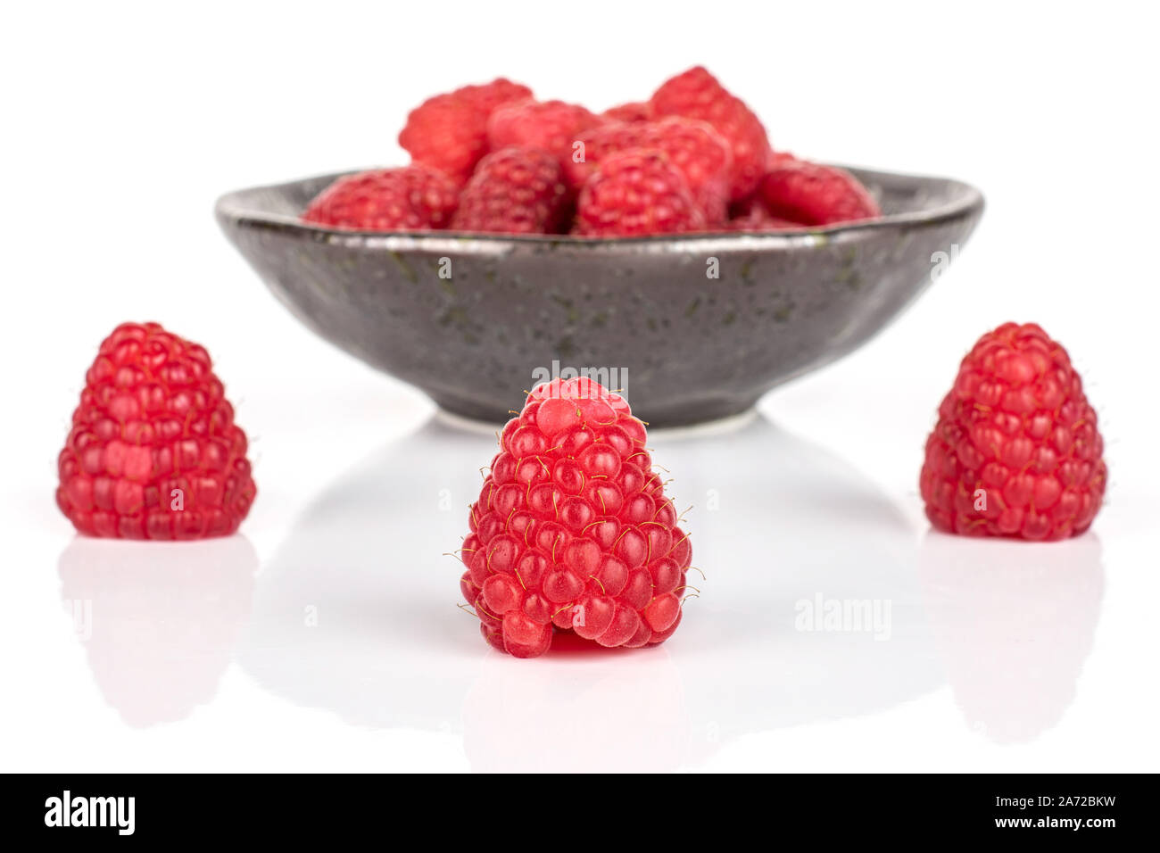 Lot of whole fresh red raspberry in dark ceramic bowl isolated on white ...