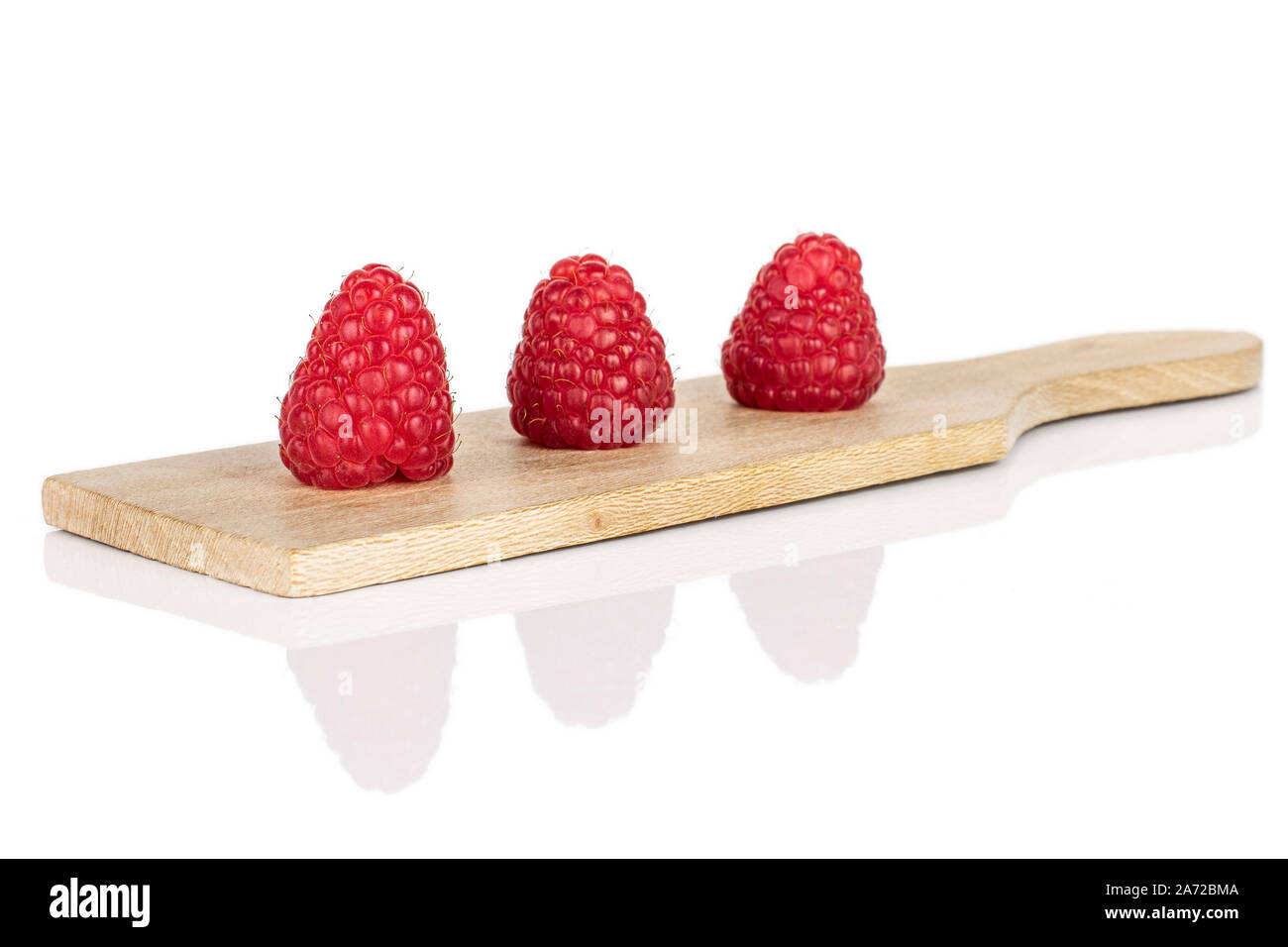 Group of three whole fresh red raspberry on small wooden cutting board ...