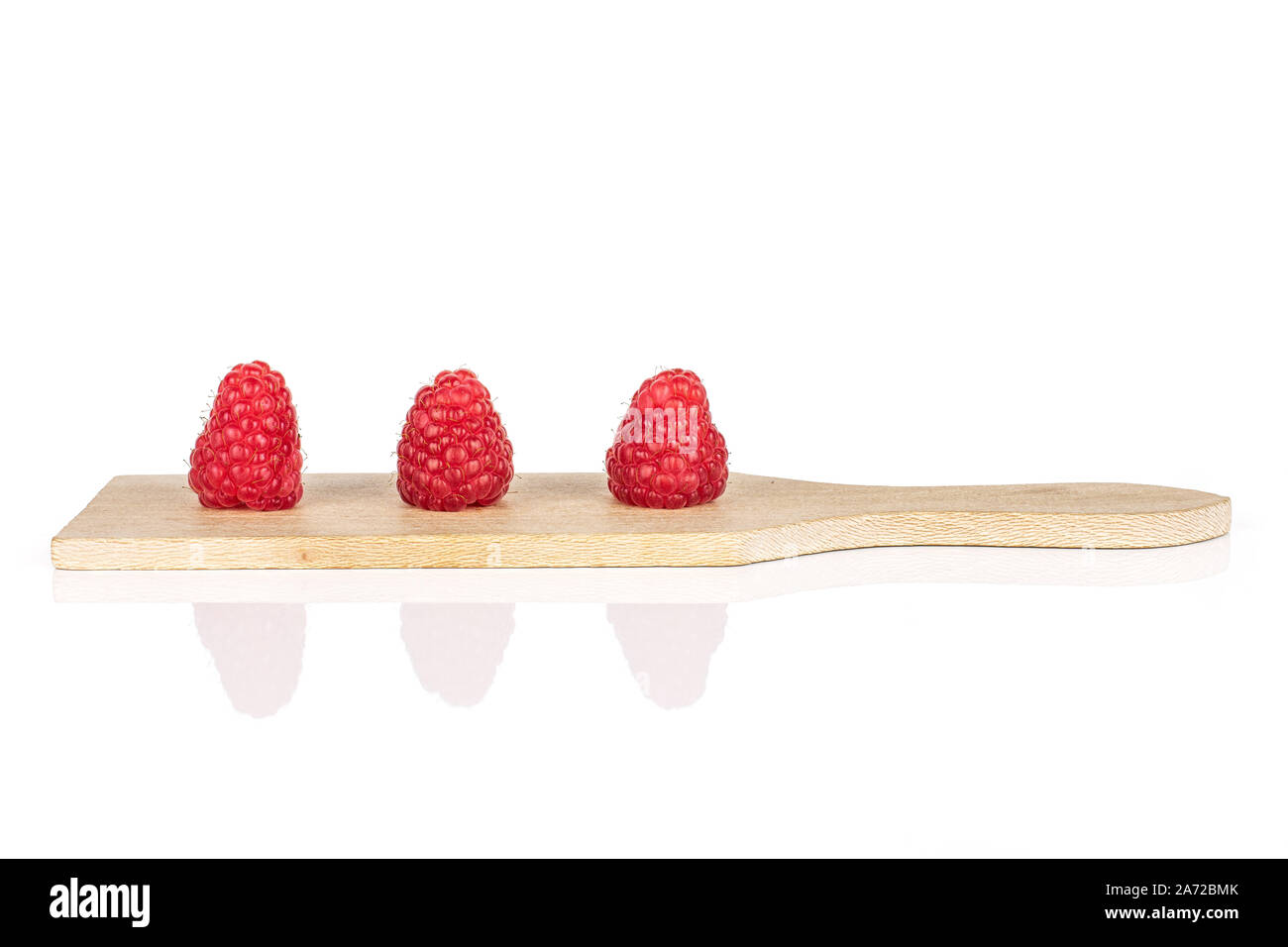 Group of three whole fresh red raspberry on small wooden cutting board ...