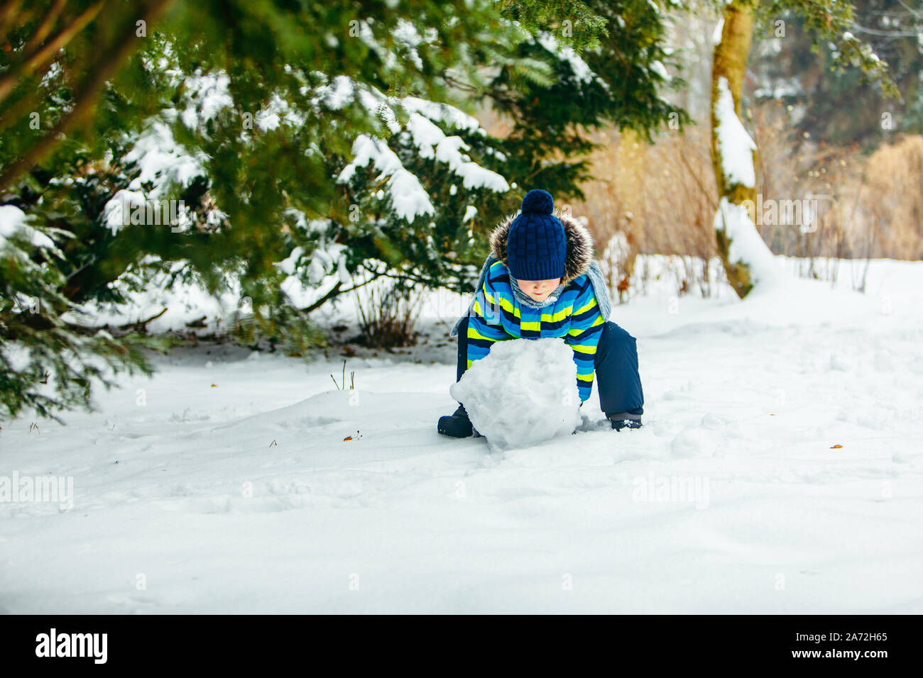 little cute boy making snowman. rolling big snowball Stock Photo - Alamy