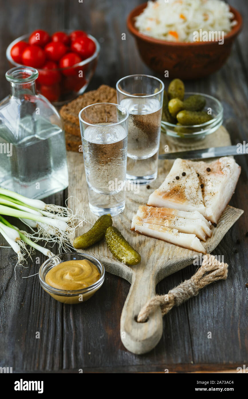 Vodka with lard, salted vegetables on wooden background. Alcohol pure ...