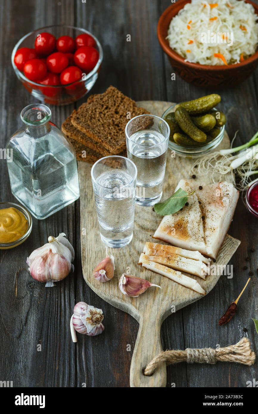 Vodka with lard, salted vegetables on wooden background. Alcohol pure ...