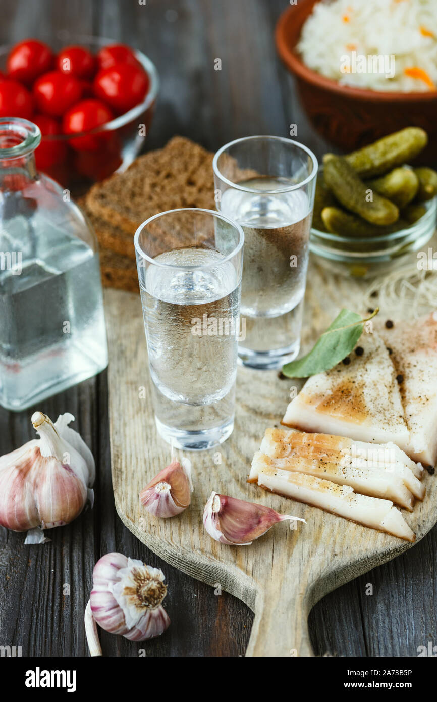 Vodka with lard, salted vegetables on wooden background. Alcohol pure ...