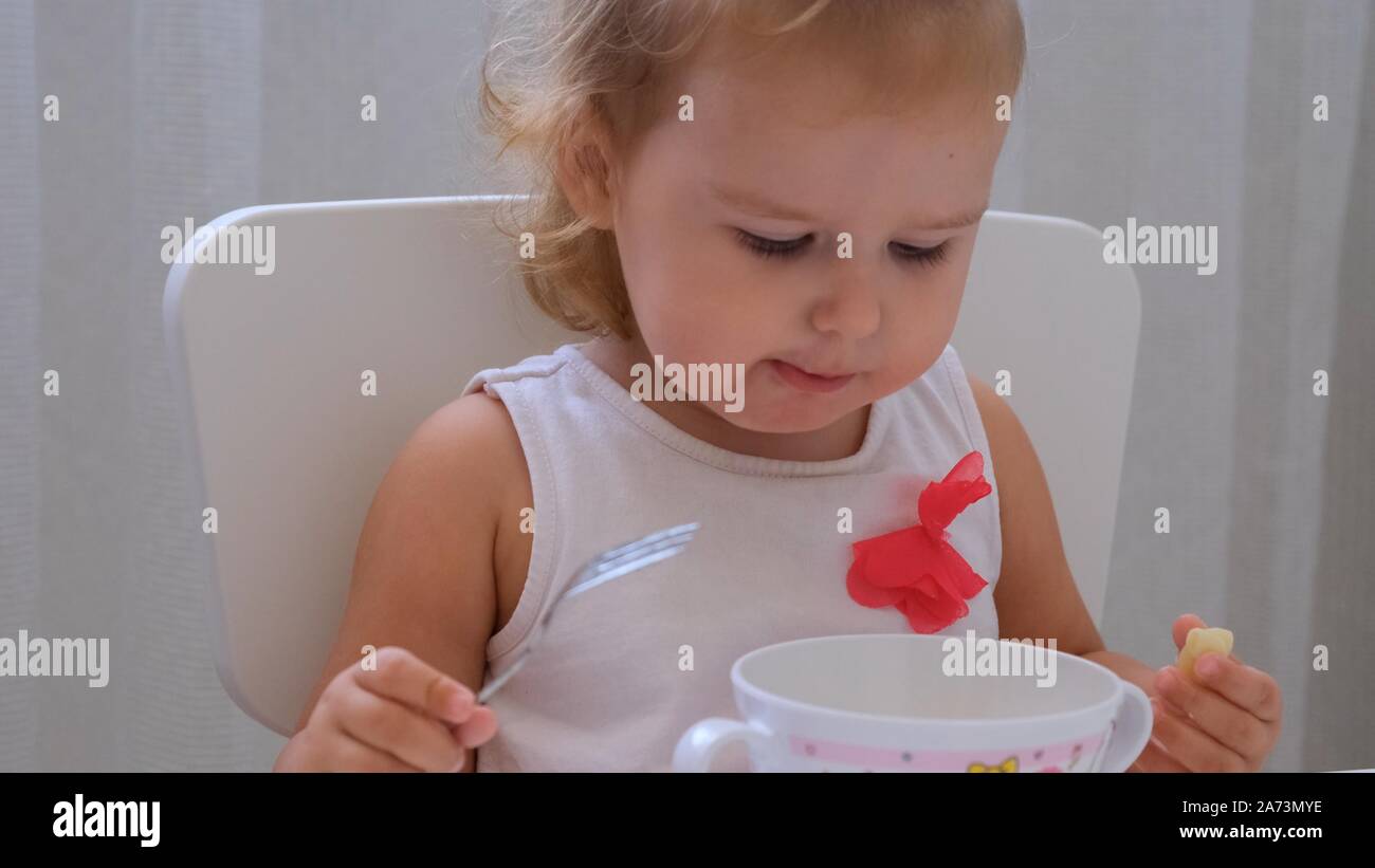 Infant girl eating baby food at a small childrens table on a white ...