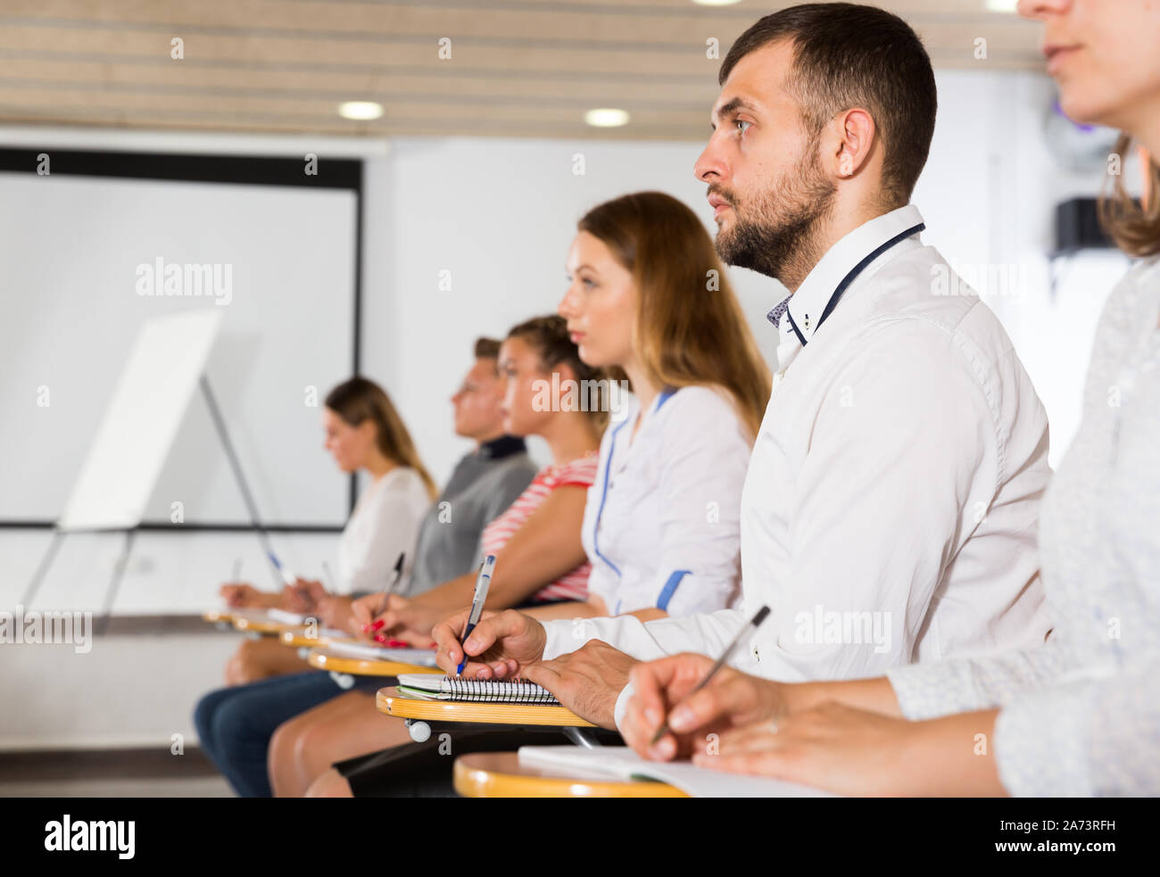 Side view of student group working on lecture in classroom, making ...