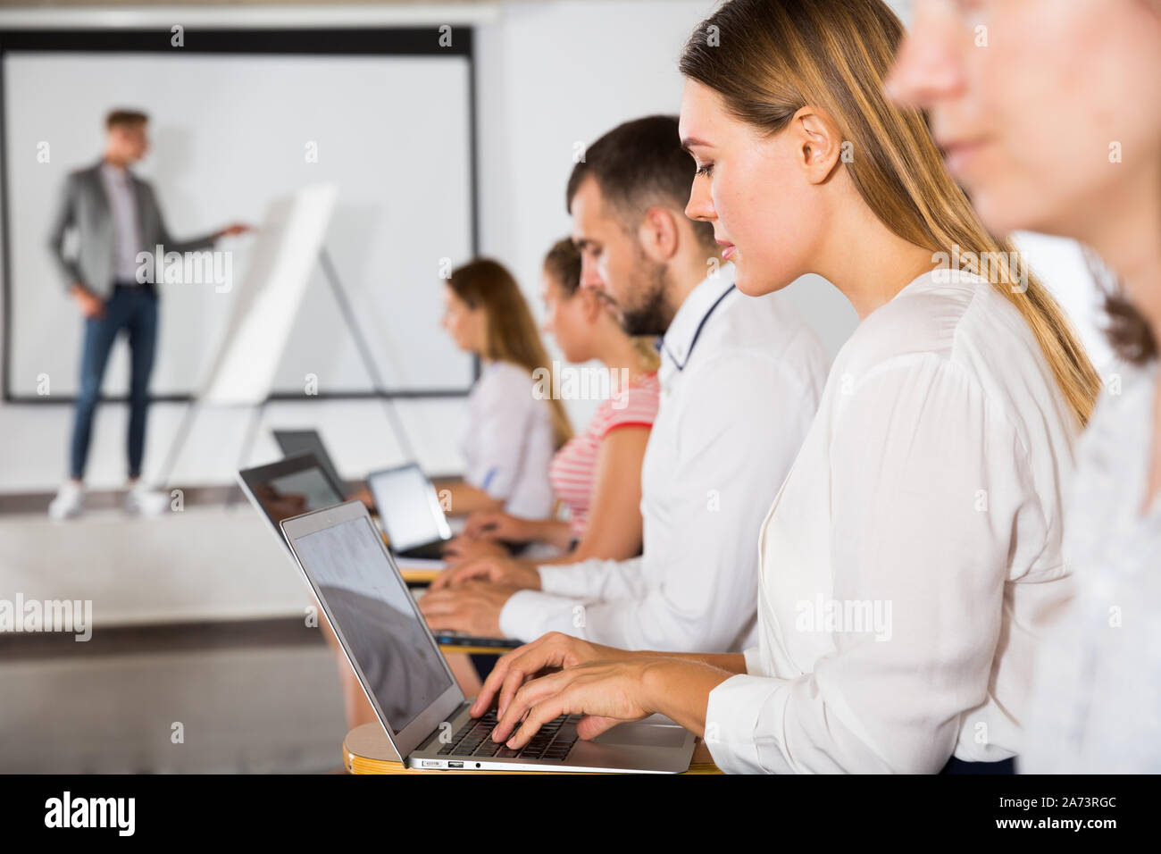 Side view of student group working with laptops on lecture in classroom ...