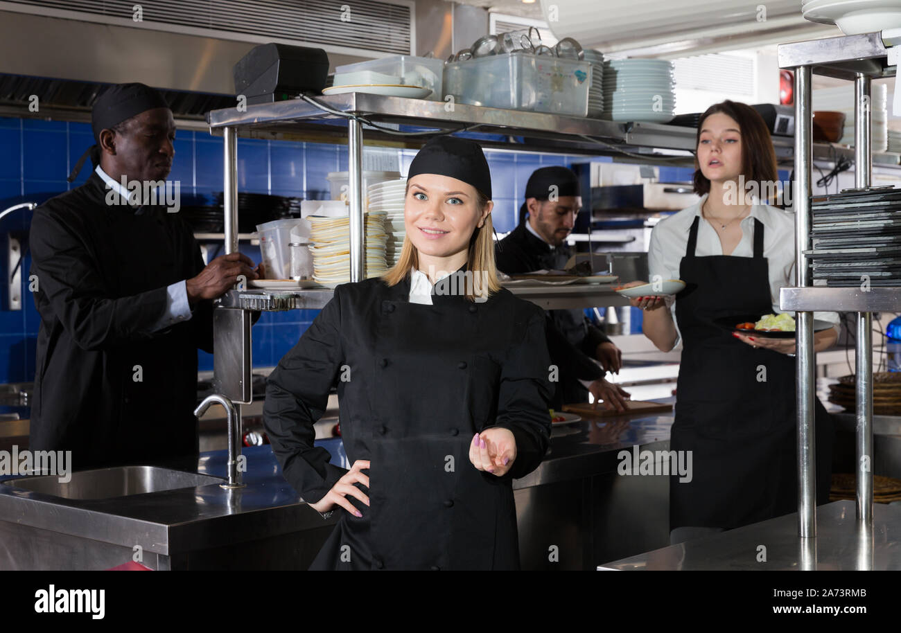 Attractive female chef of restaurant standing in professional kitchen ...