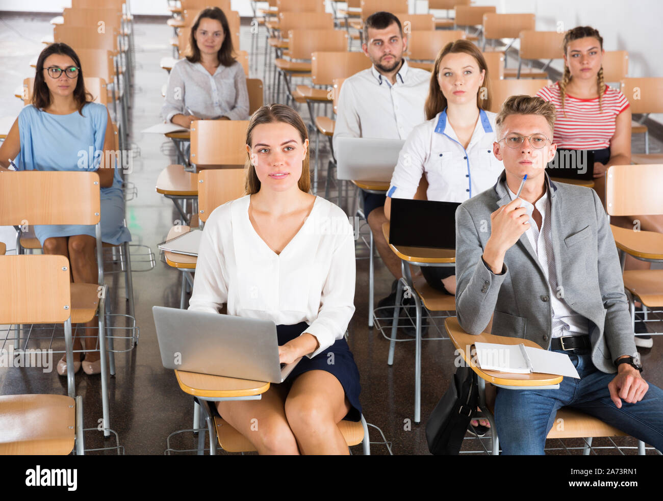 Portrait of group of people sitting with laptops in lecture hall at ...