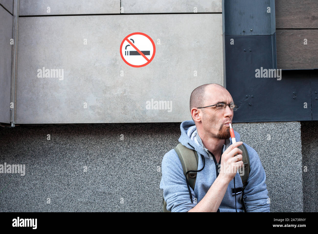 Portrait of caucasian man smoke electronic cigarette under sign No ...