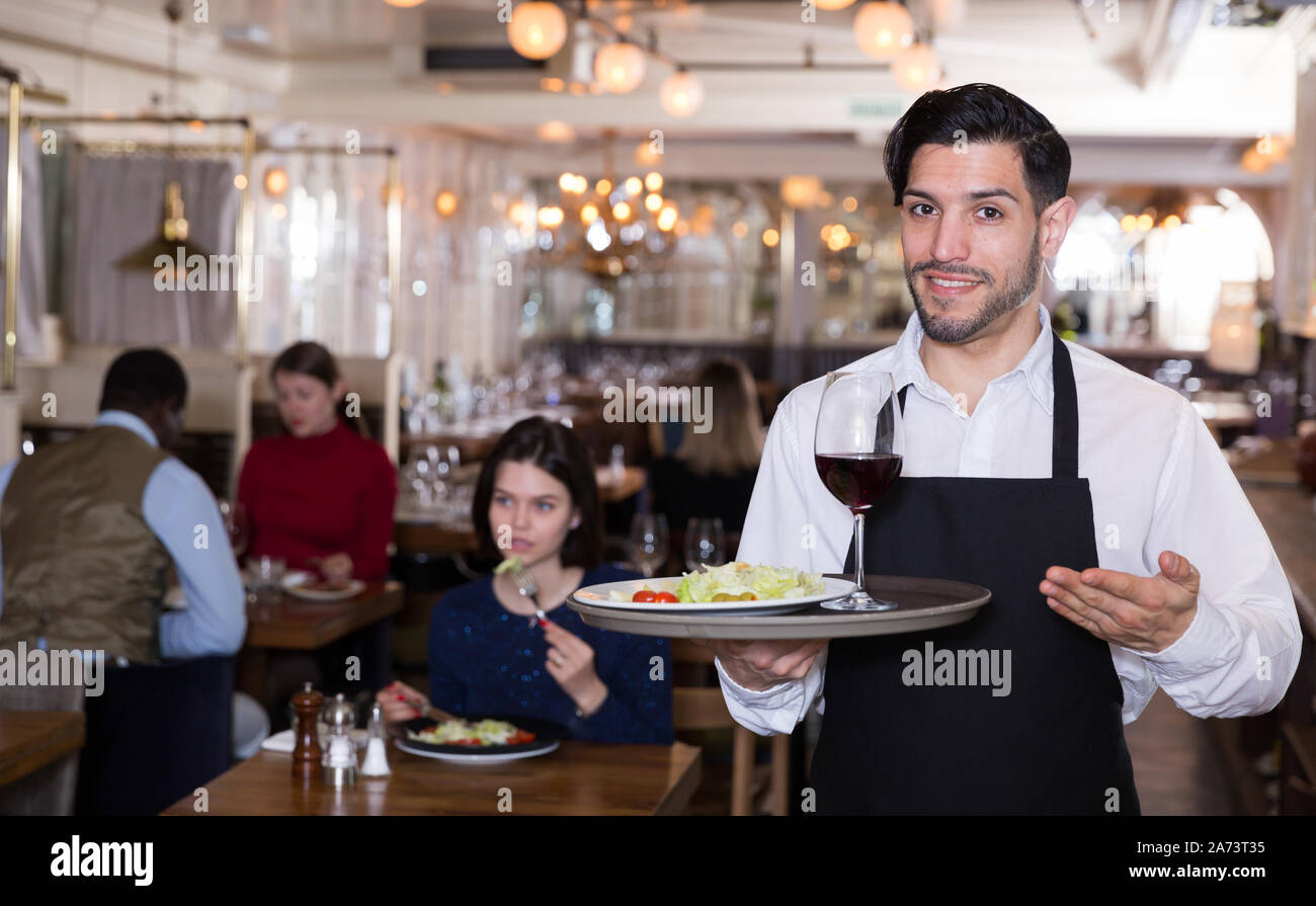 Confident waiter with serving tray offering dishes in modern cozy ...