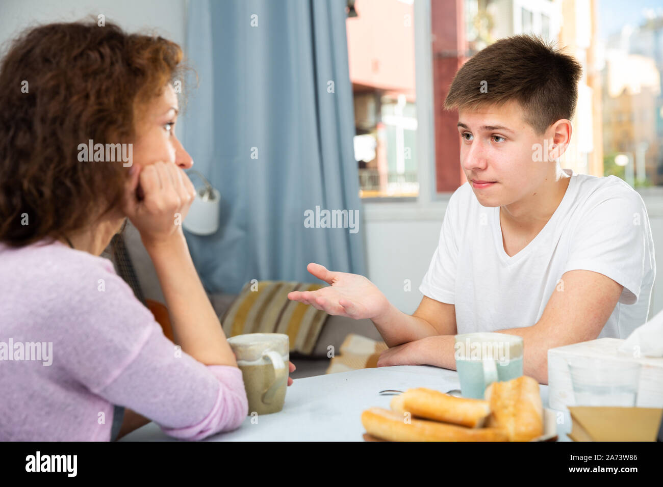 Cheerful teenage boy telling interesting story to his mother at home ...
