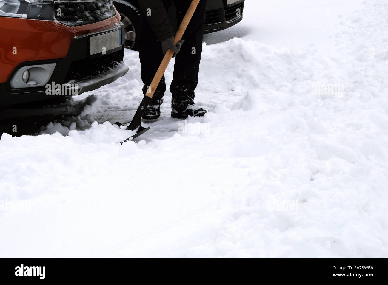 Man brushing and shoveling snow from orange car in winter after ...