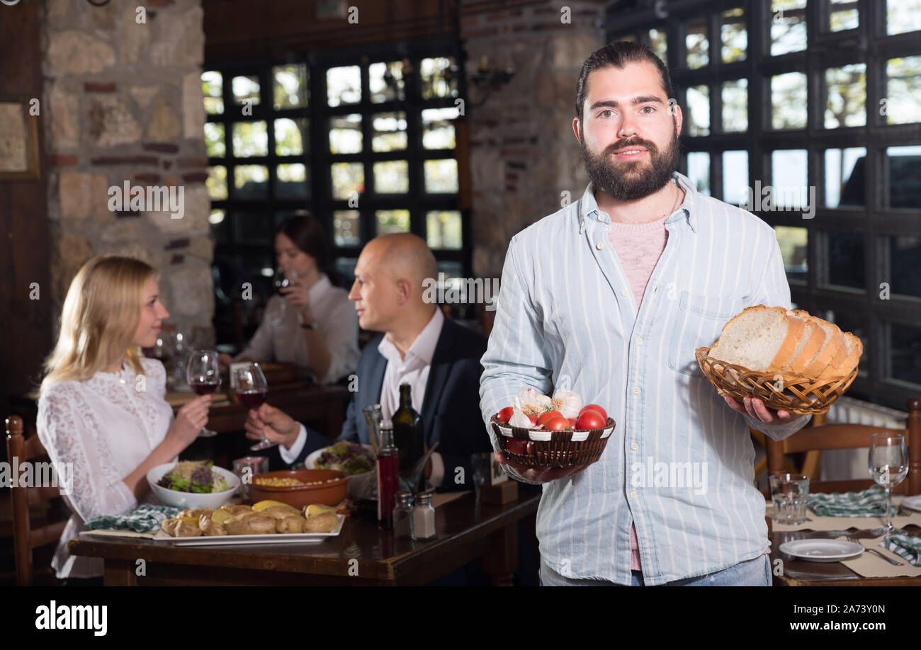 Positive male waiter welcoming guests to country restaurant Stock Photo ...