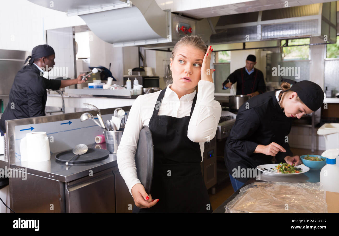 Unhappy and tired young waitress waiting ordered dishes in restaurant ...