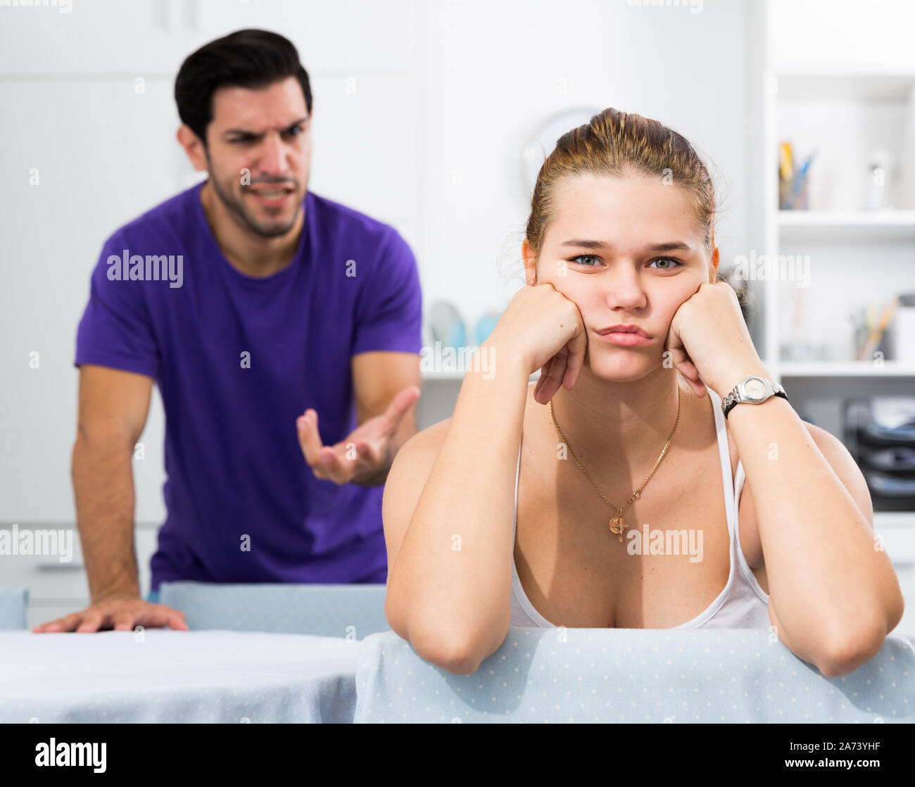Frustrated girl sitting at home table on background with angry ...