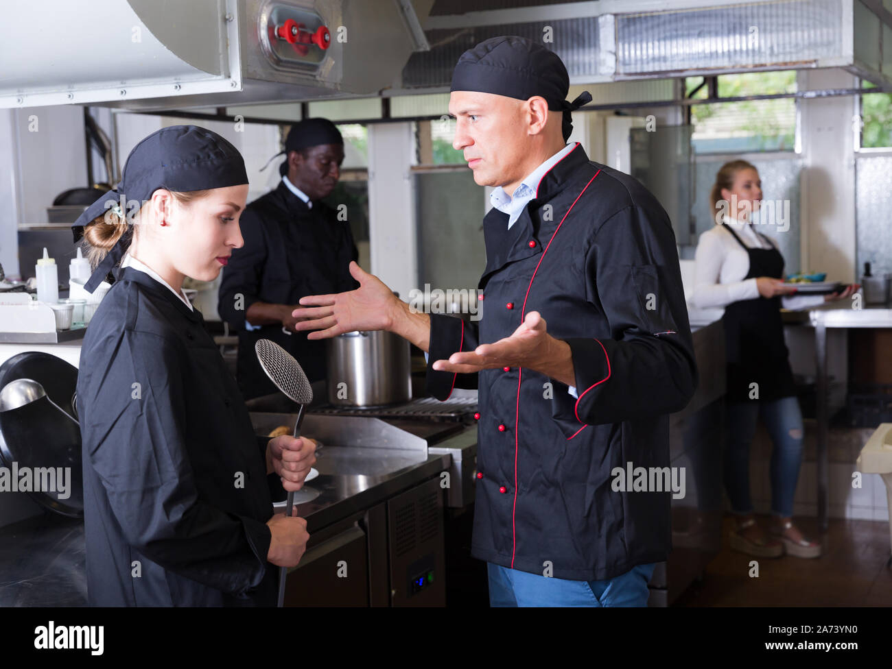 Angry male chef talking to his female assistant in commercial kitchen ...