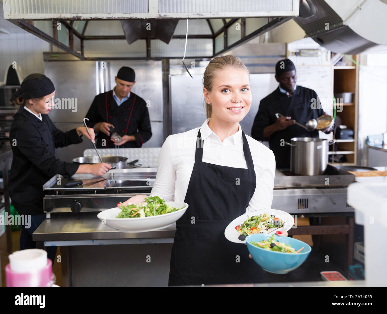 Portrait of attractive waitress with ordered dishes in kitchen of ...