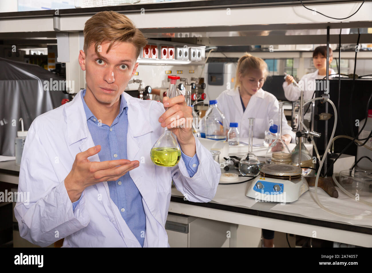 Portrait of young male scientist holding flask of reagent at ...