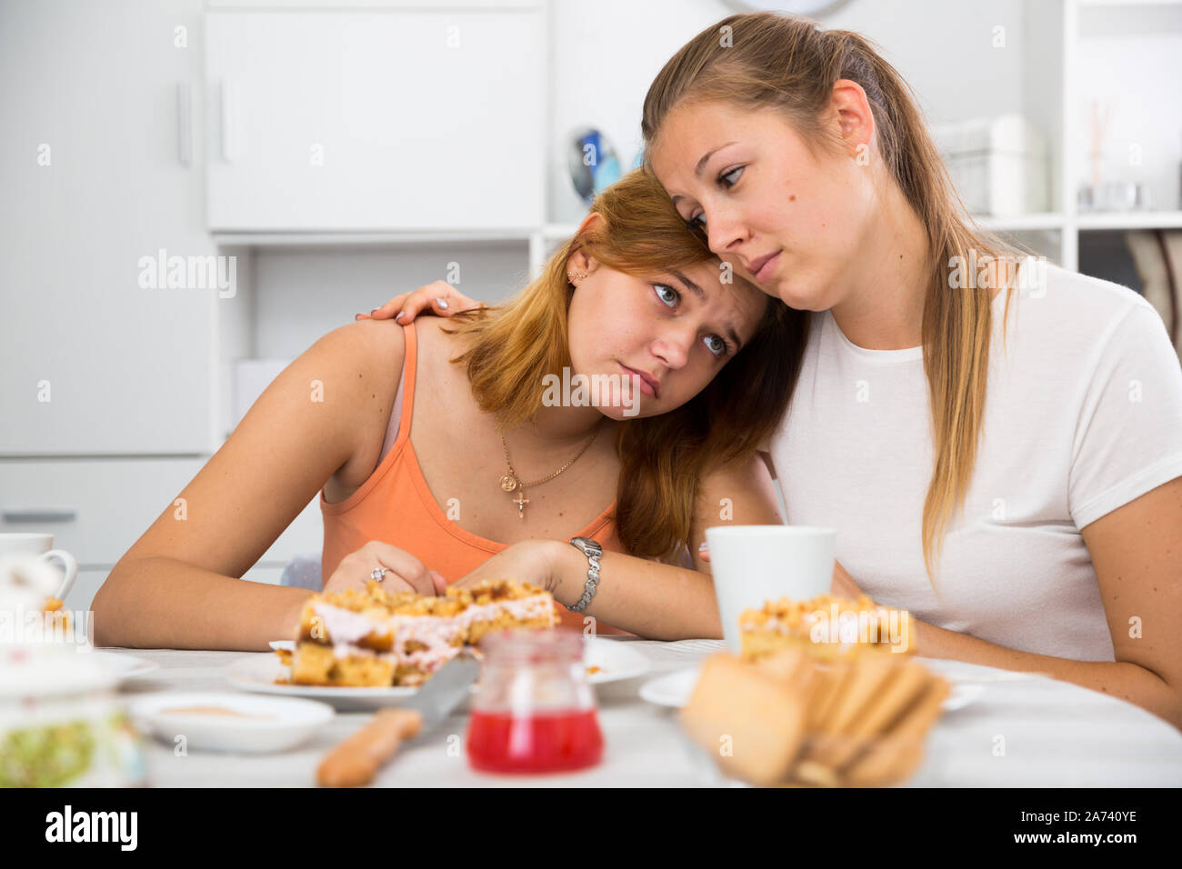 Female talking with young sad friend at the table with cake at home ...