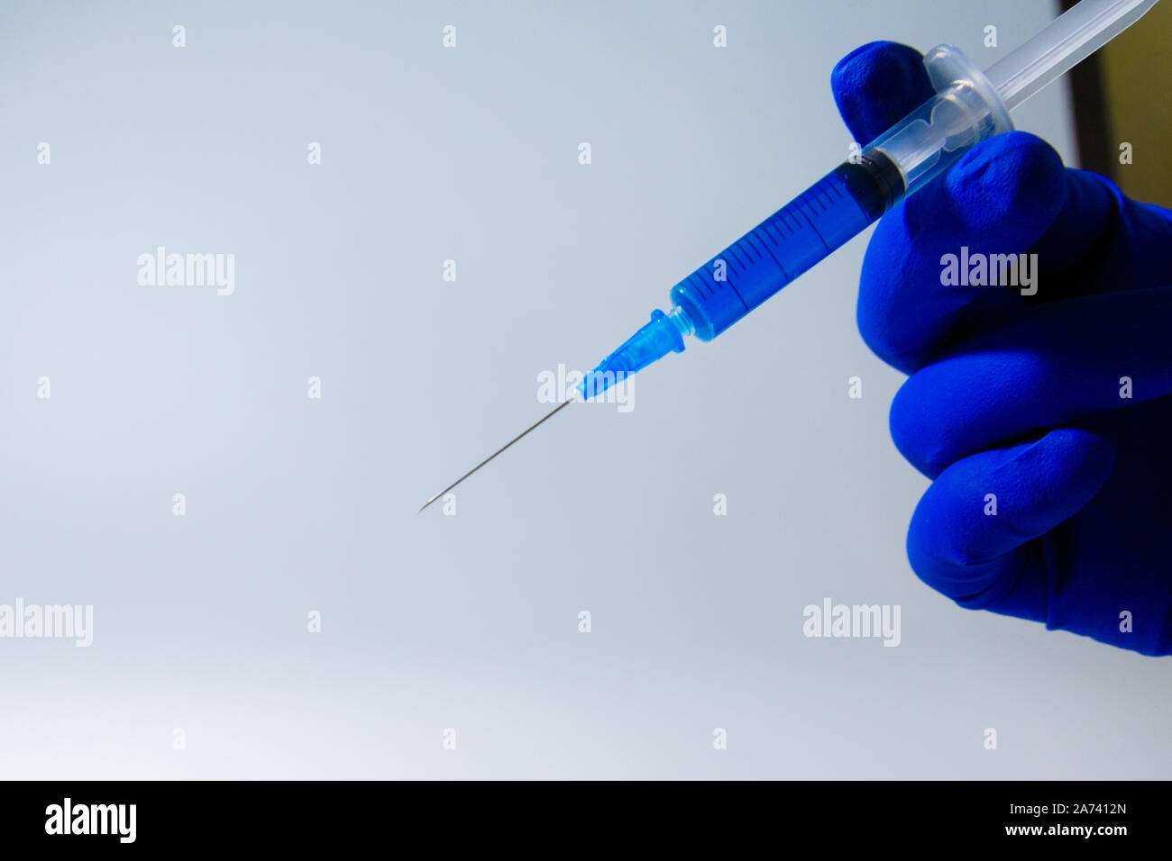 A medical syringe in his blue-gloved hand. A syringe with a blue liquid ...