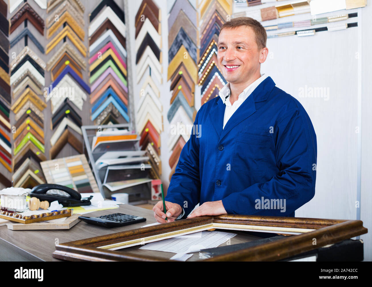 Smiling positive diligent man worker holding picture frame details on ...