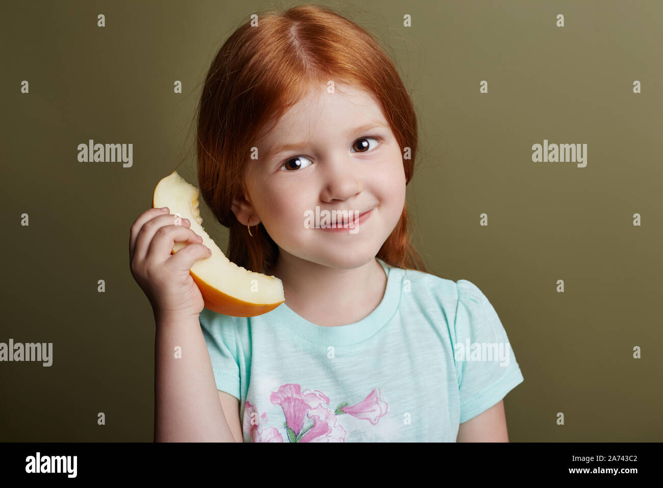Little girl eats a melon on a green background, bright cheerful ...