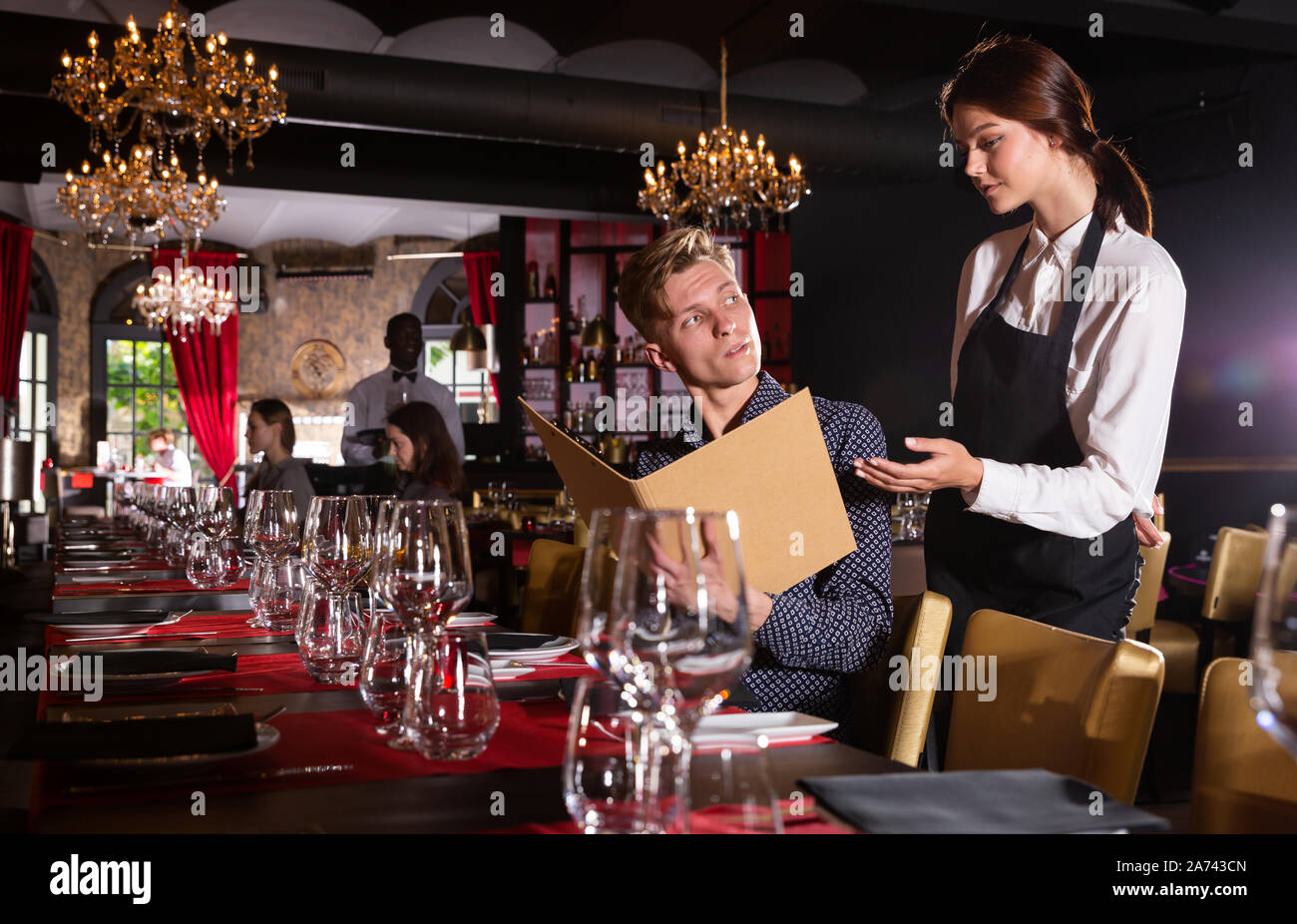 Portrait of handsome young man holding menu and ordering food in luxury ...