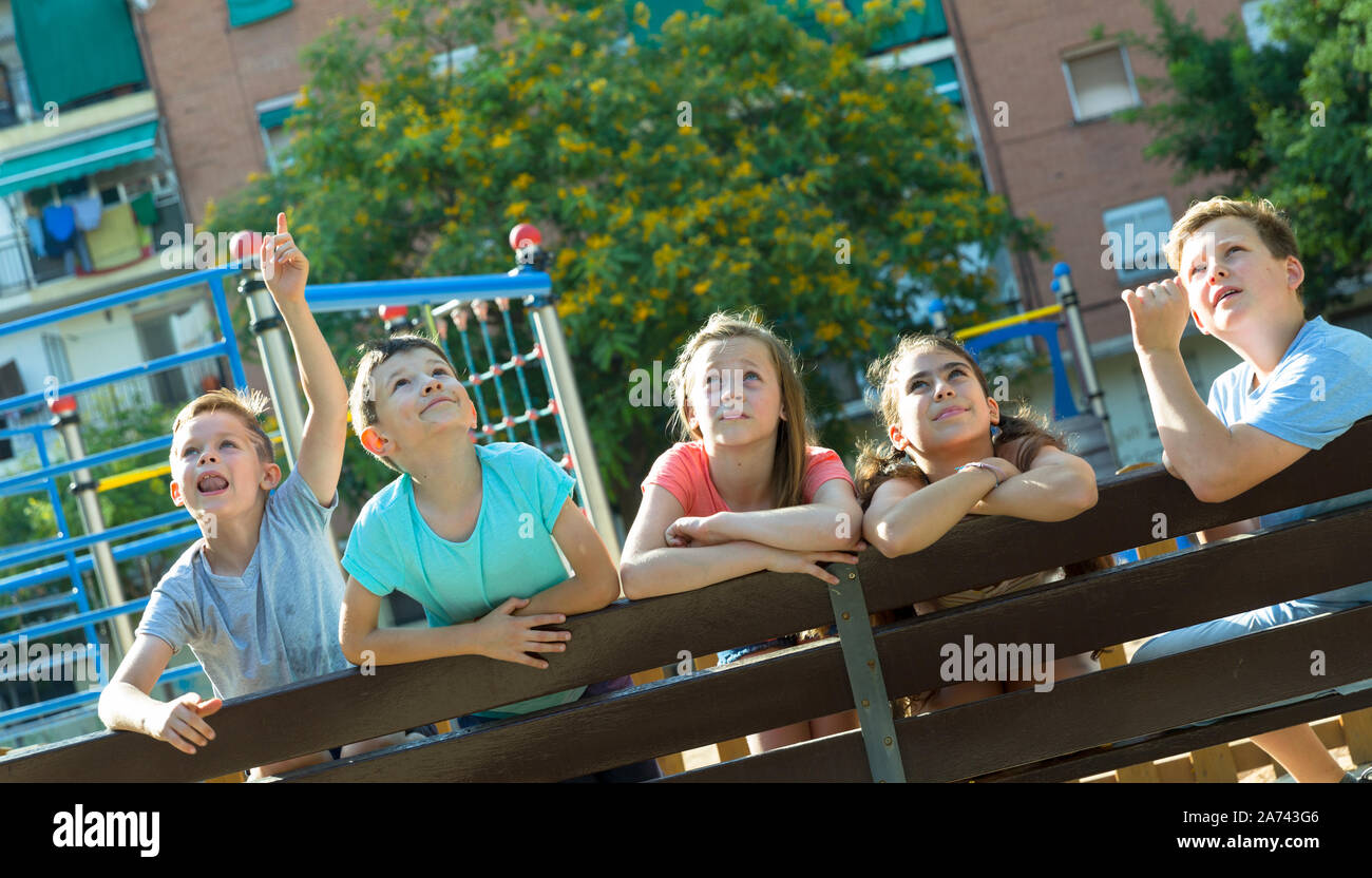 Five glad children sitting on a bench at the playground and point to ...