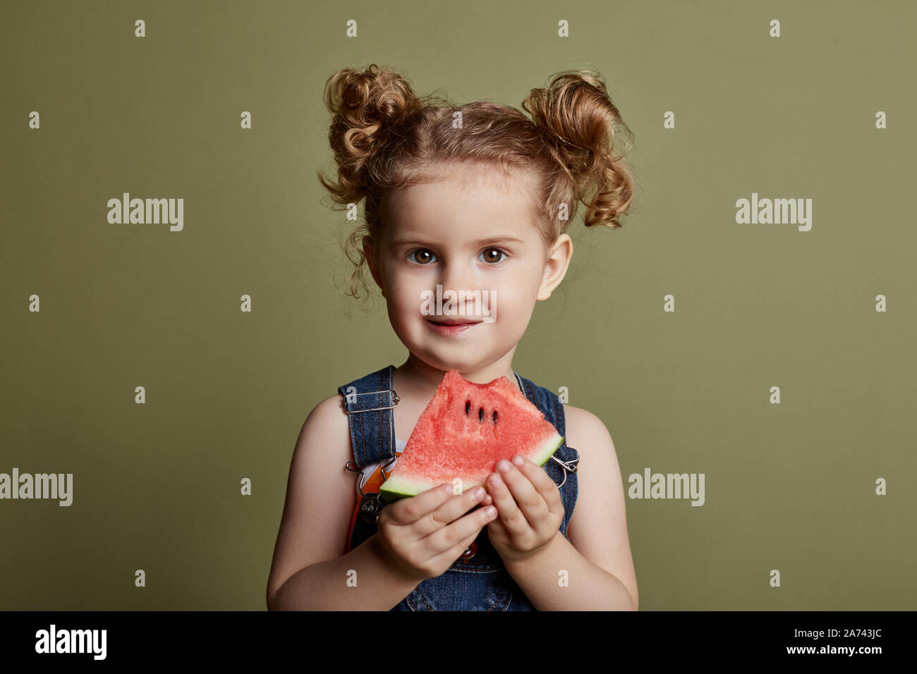 Little girl eats a watermelon on an olive background, bright cheerful ...
