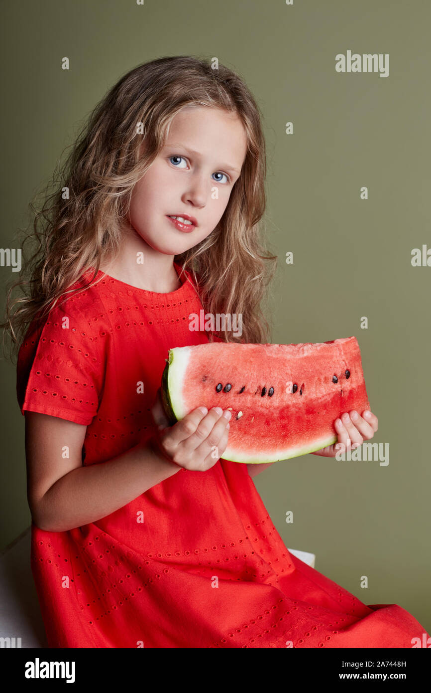 Little girl eats a watermelon on an olive background, bright cheerful ...