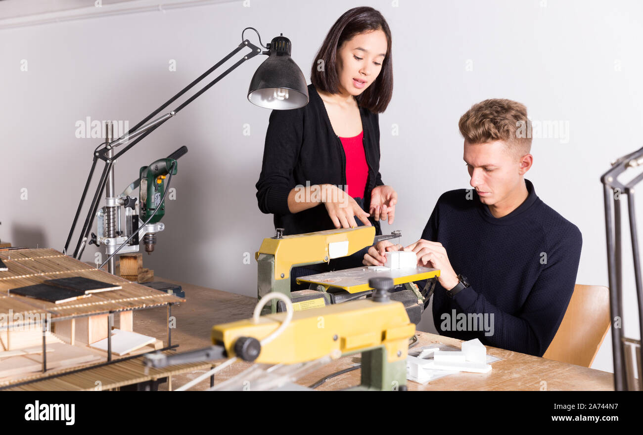 Young female architect helping male colleague making elements on scroll ...