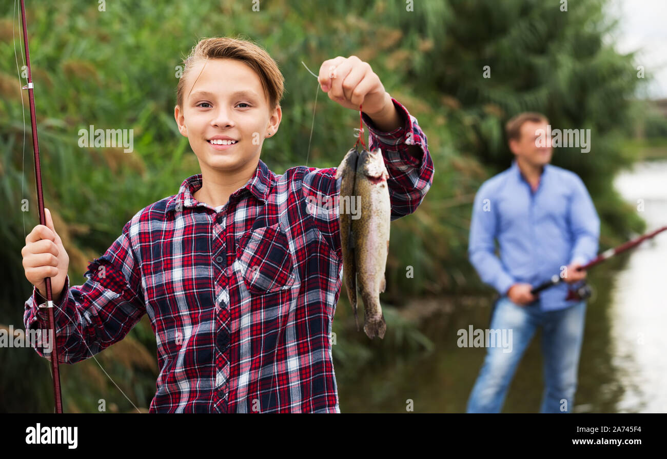 Portrait of positive teenager boy showing catch fish he holding in ...