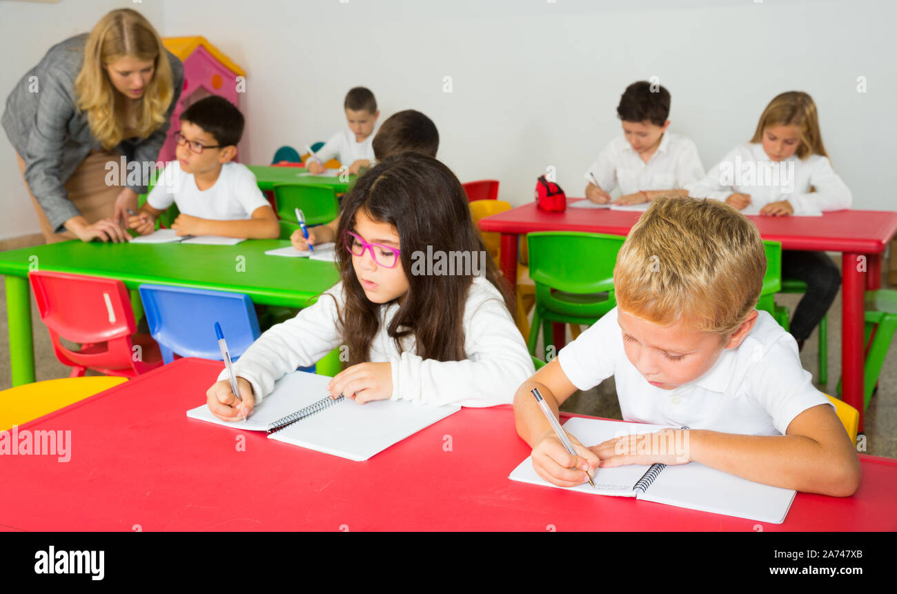 Female teacher helping schoolchildren doing their task in classroom ...