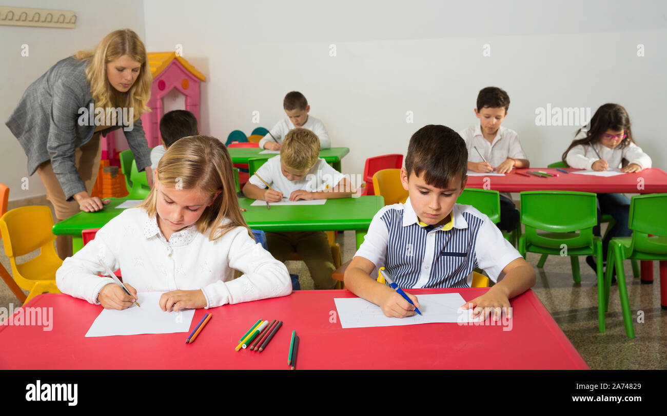 Group of school kids with pens and notebooks studying in classroom with ...